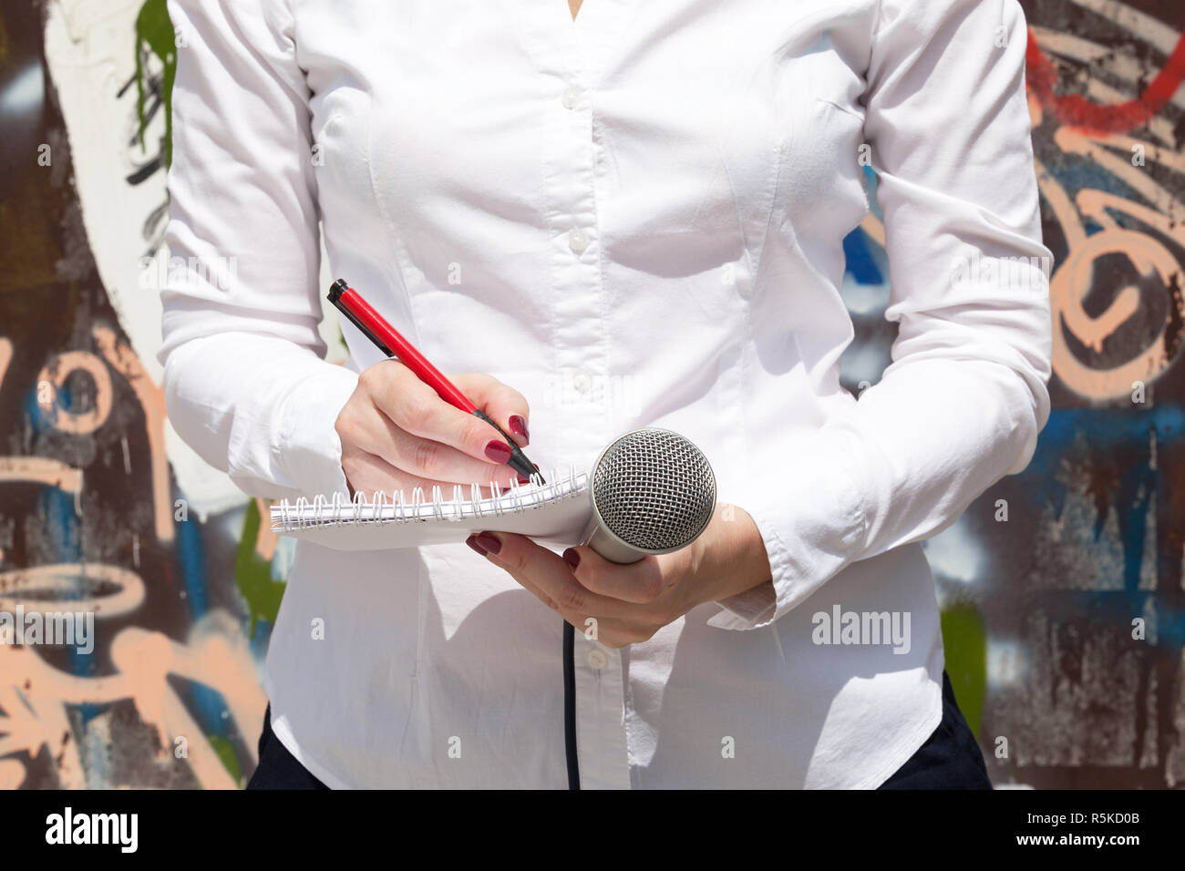 Female journalist at news event, writing notes, holding microphone ...
