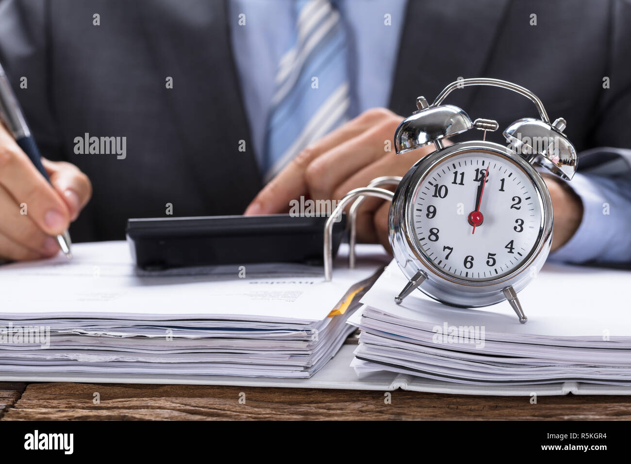 Businessman Calculating Invoice With Alarm Clock On Documents Stock ...