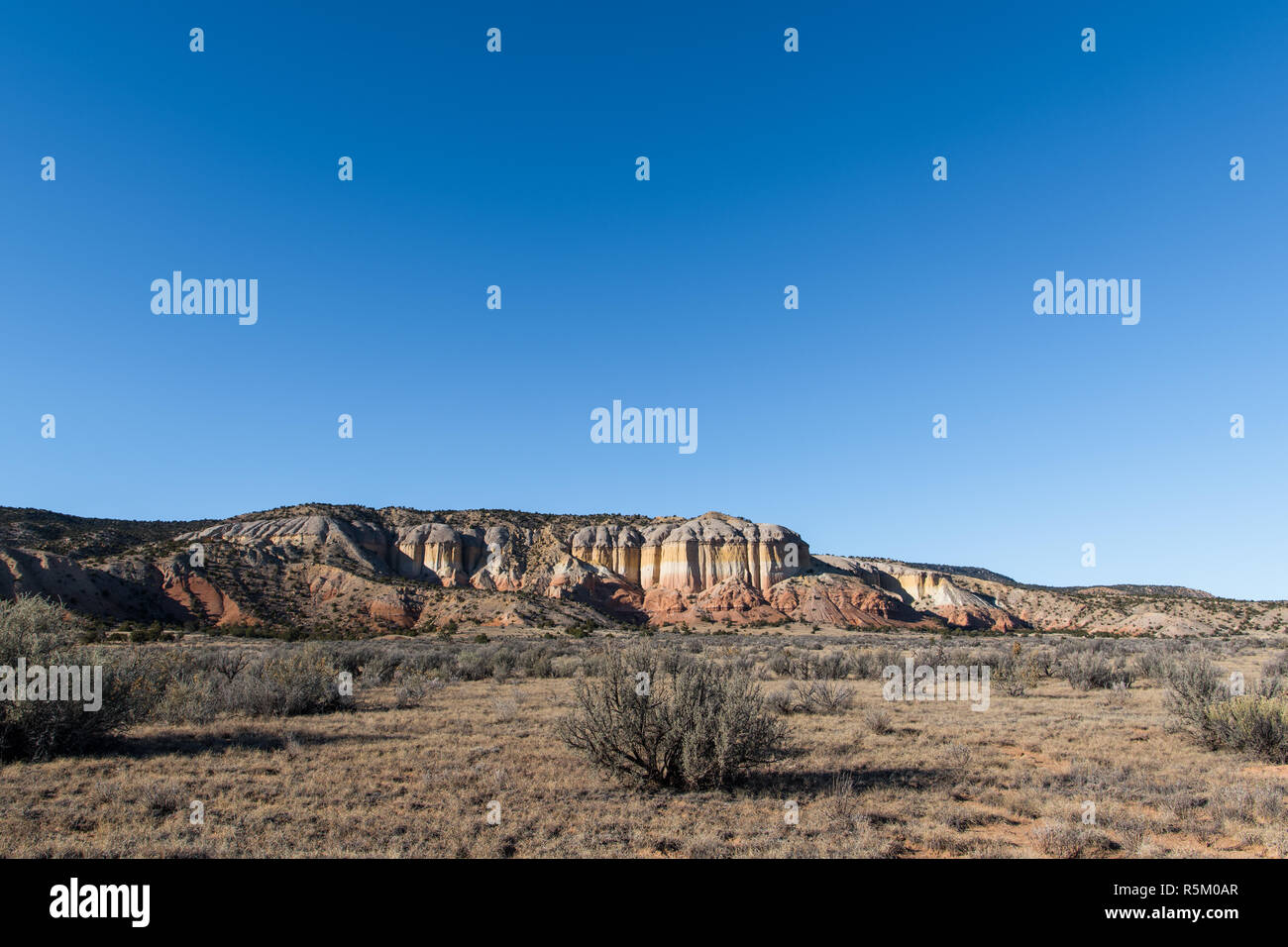 Landscape of grassy plain, sagebrush, and colorful cliffs under a vast ...