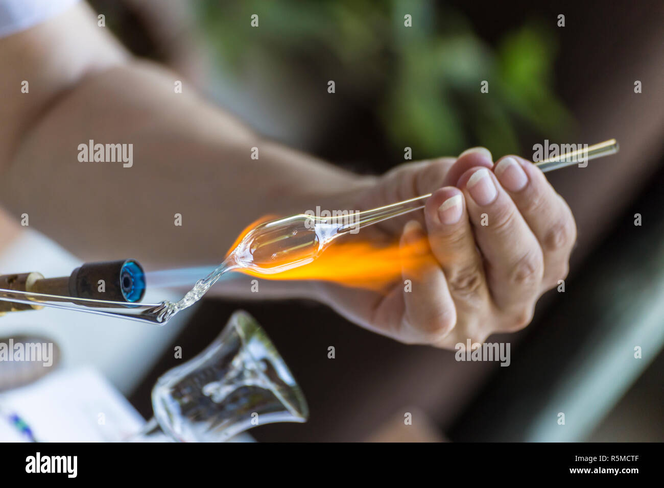 Craftsman melting and shaping a piece of glass on a small blue torch ...