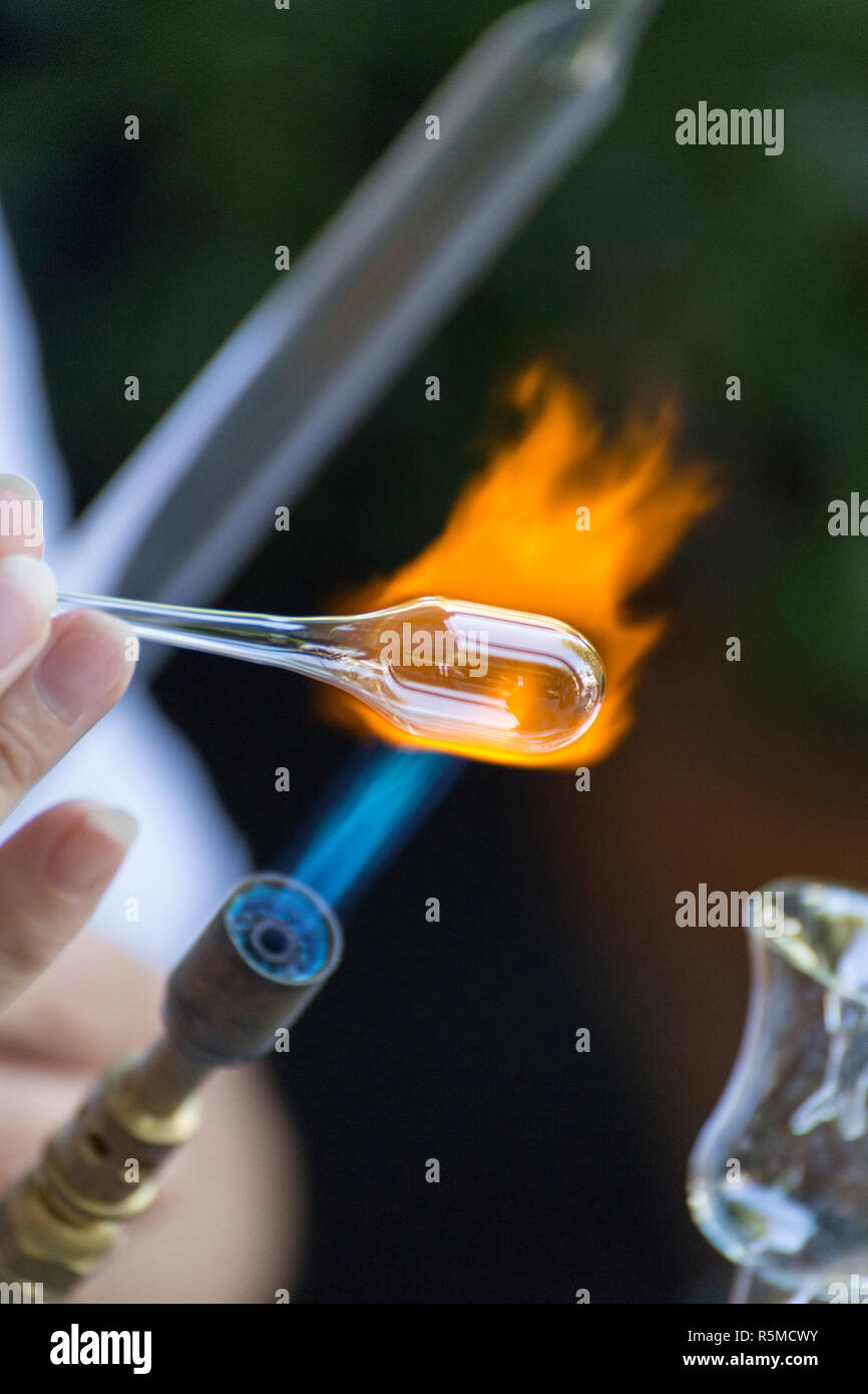 Craftsman melting and shaping a piece of glass on a small blue torch ...