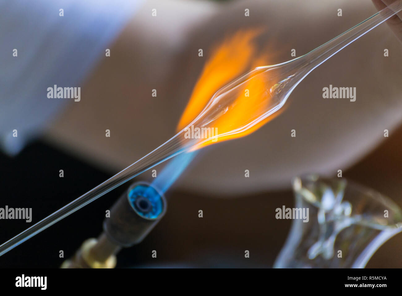 Craftsman melting and shaping a piece of glass on a small blue torch ...