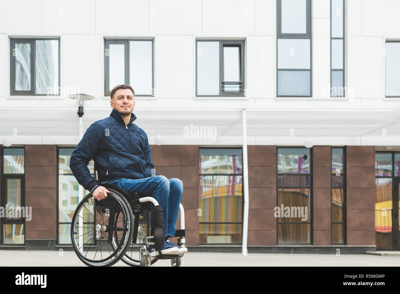 Young man in a wheelchair against the backdrop of a modern high-rise ...