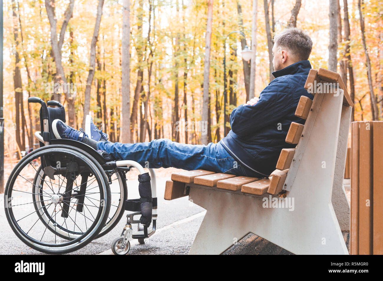 Young man resting sitting on a bench with his legs on his wheelchair ...
