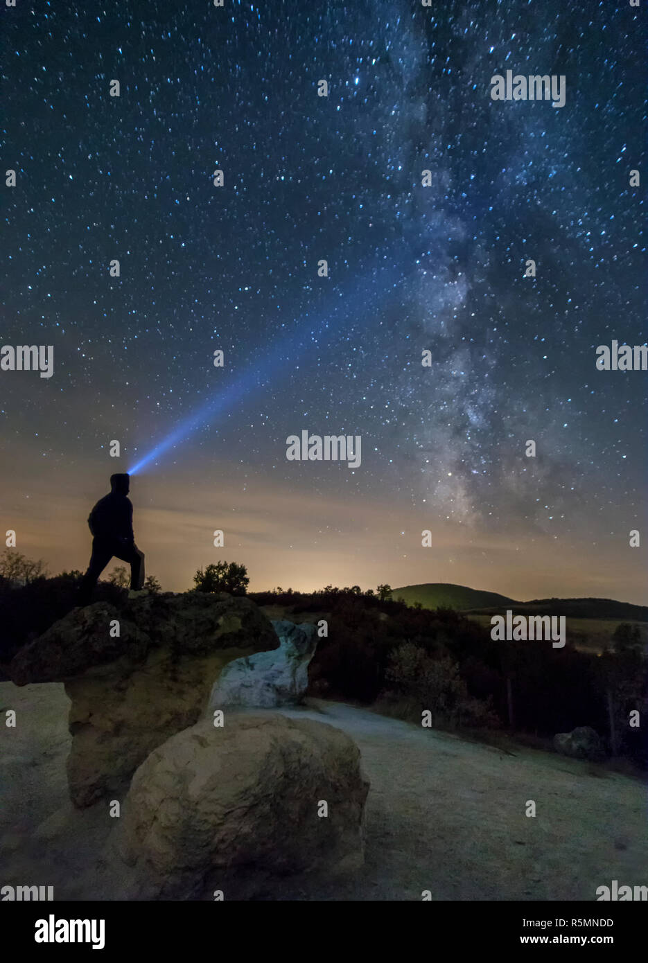 Man standing on a rock with a flashlight trying to light up the night ...