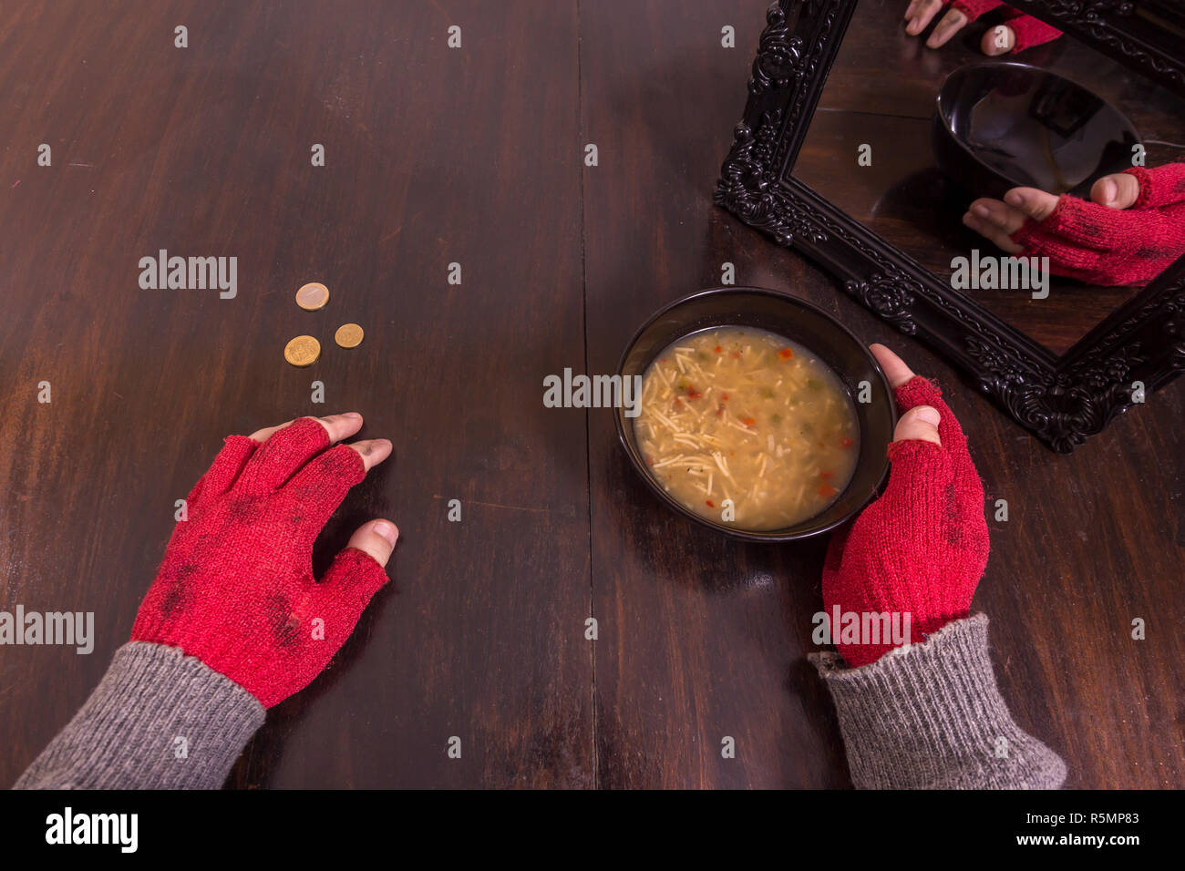 Hands with red gloves taking a bowl of soup from a worn out table ...
