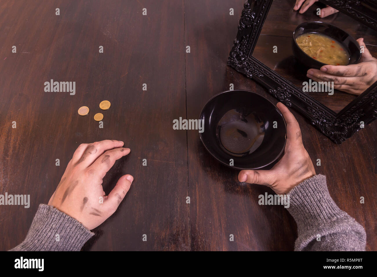 Hands taking a bowl of soup from a worn out table. Poverty and illusion ...