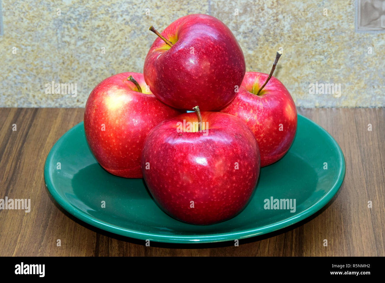 Pile of white-spotted red apples on a green plate over a brown wooden ...