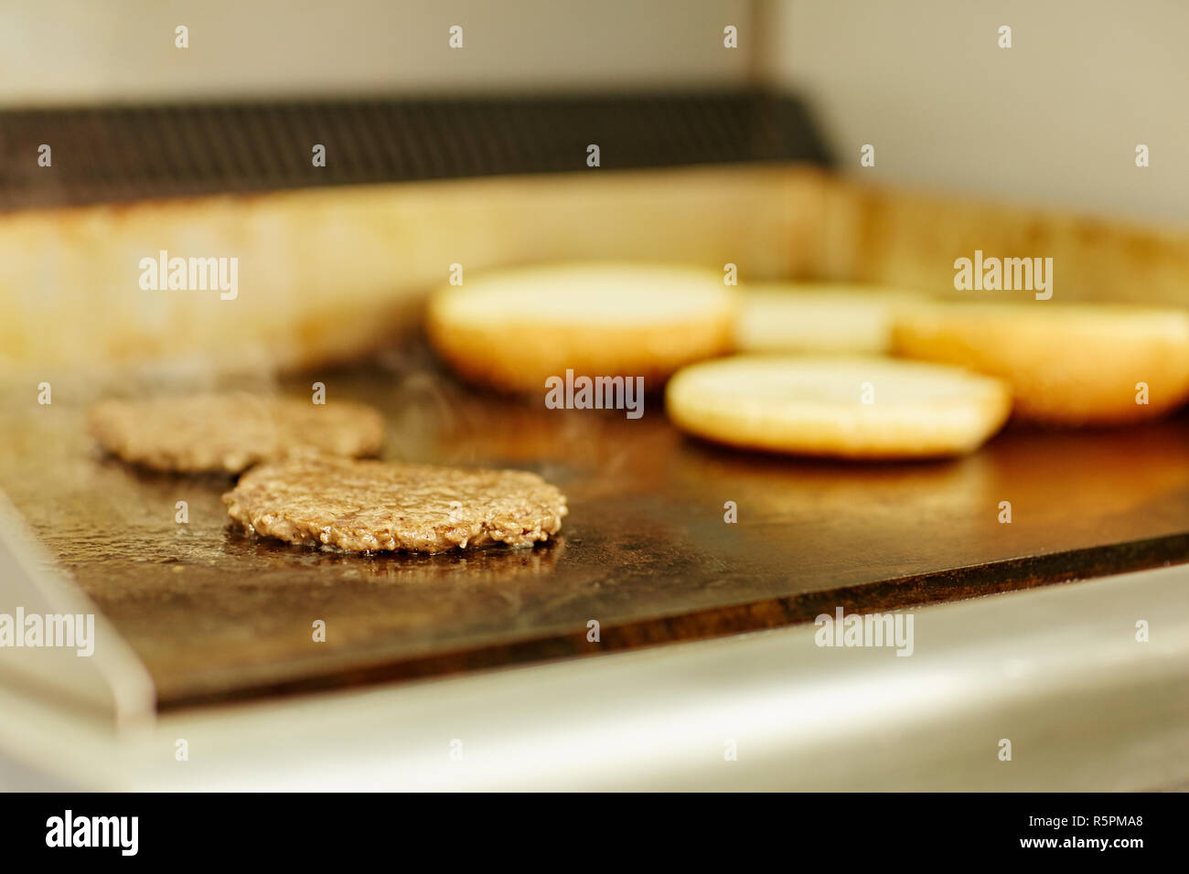 Burger patties being fried alongside open buns being toasted Stock ...