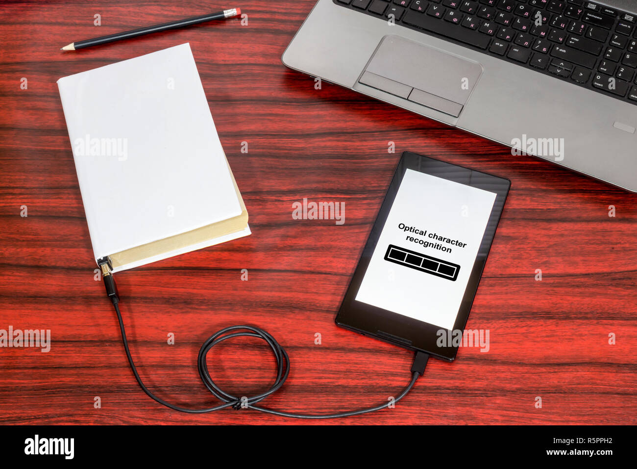 Book connected to a tablet through an USB cable on a desk. Optical ...