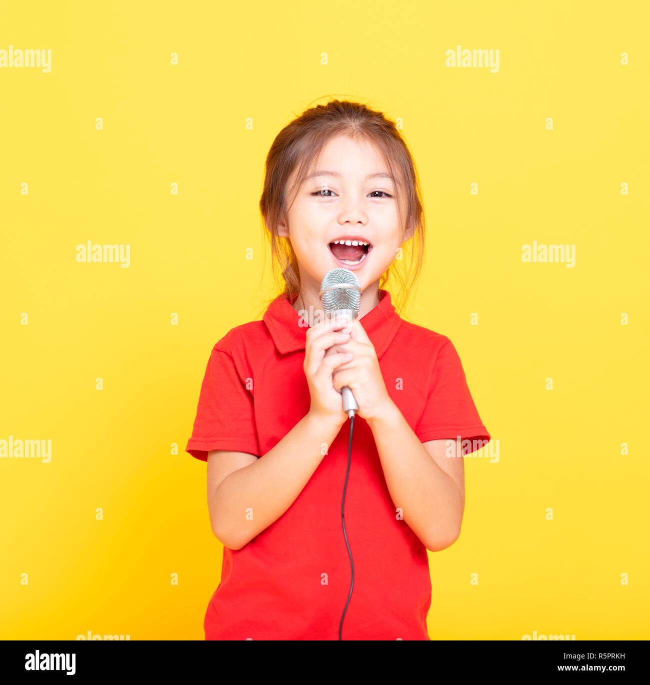 happy little girl singing on yellow background Stock Photo - Alamy