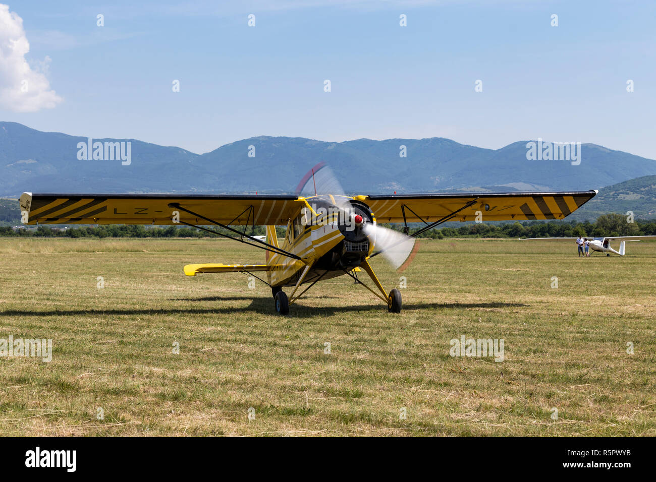 Small airplane on a grass airfield with mountains in the background ...