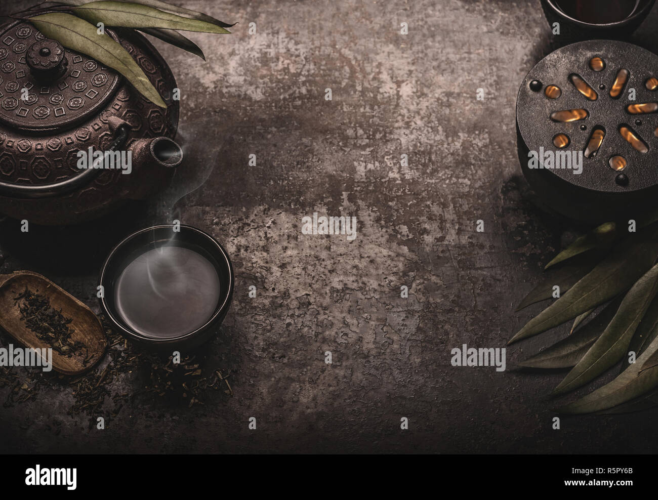 Dark asian tea background with black iron teapot and mug of green tea ...
