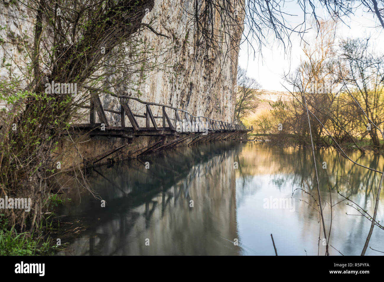 Wooden walkway hanging alongside a vertical cliff crossing a river on ...