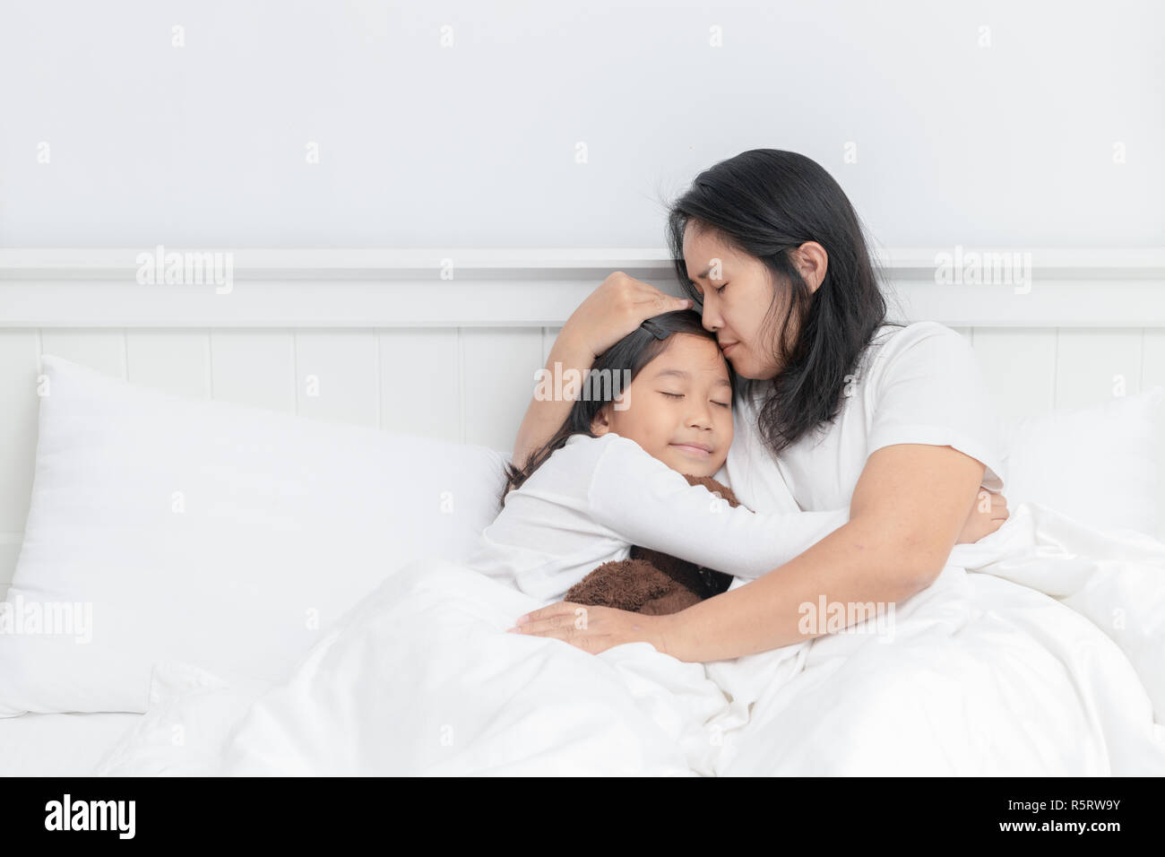 Mother hugging and kiss her daughter on bed before sleep, love and care ...
