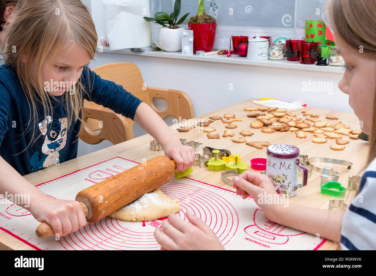 A girl is using the rolling pin to roll out the dough on the table ...