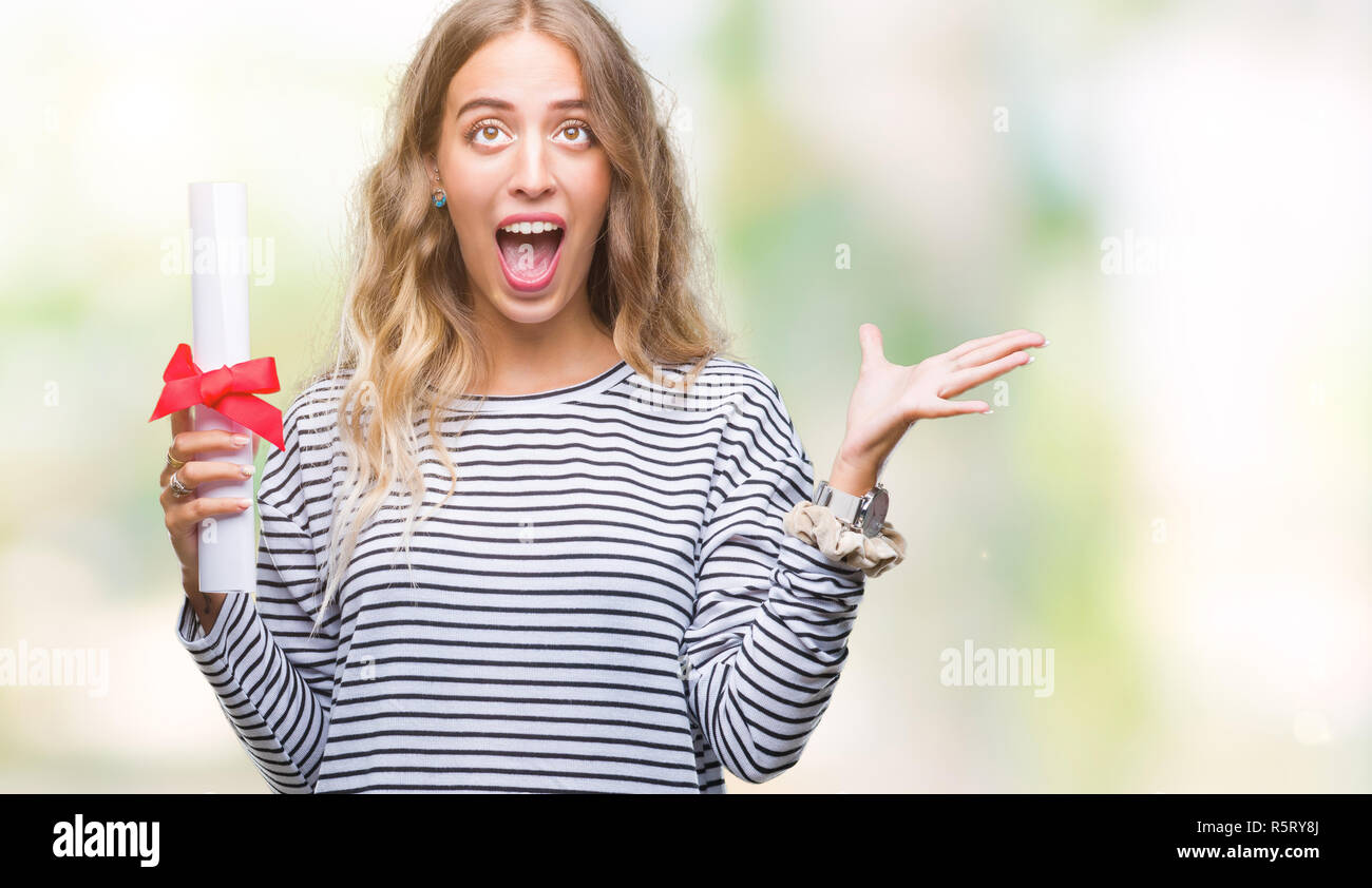 Beautiful young blonde woman holding degree certificate over isolated ...