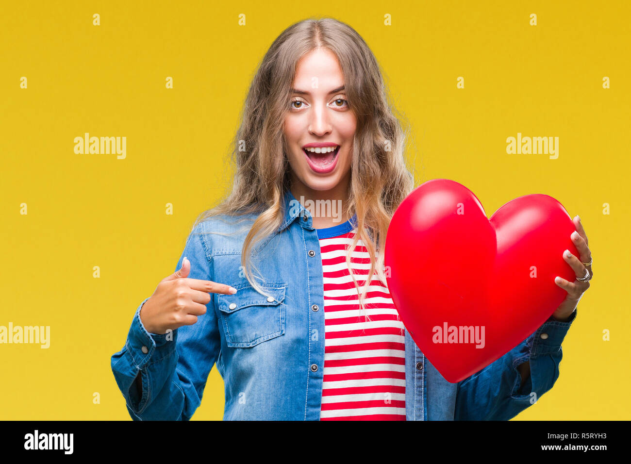 Beautiful young blonde woman holding heart valentine over isolated ...
