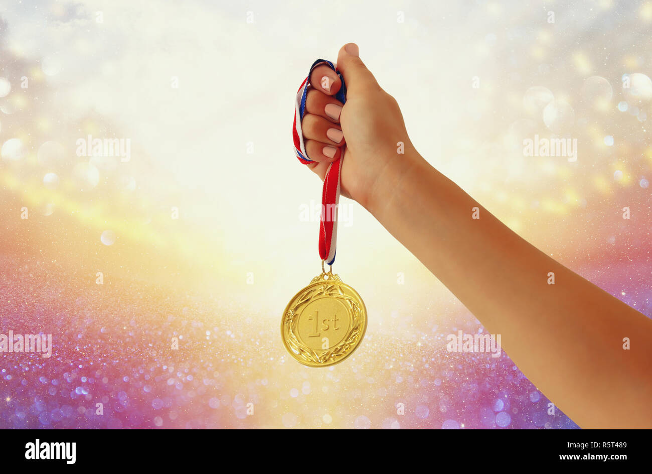 woman hand raised, holding gold medal against glitter background. award ...