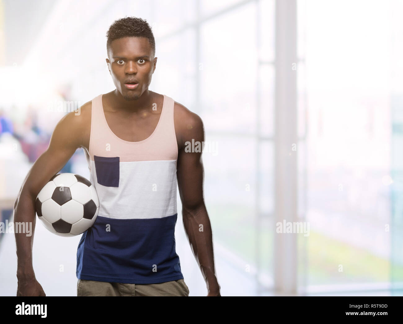 Young african american man holding soccer football ball scared in shock ...