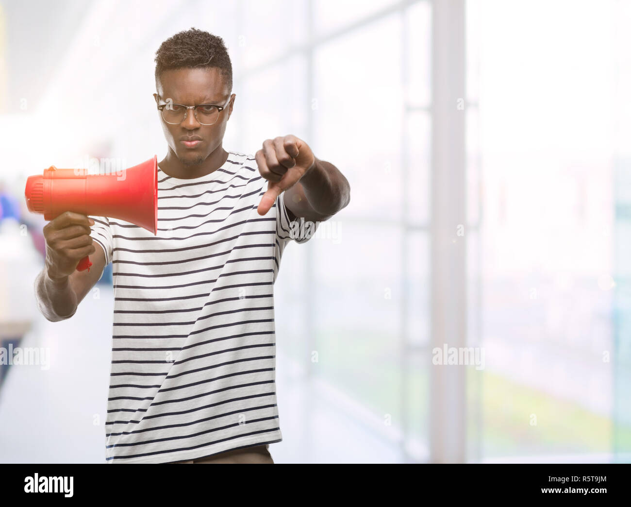 Young african american man holding megaphone with angry face, negative ...