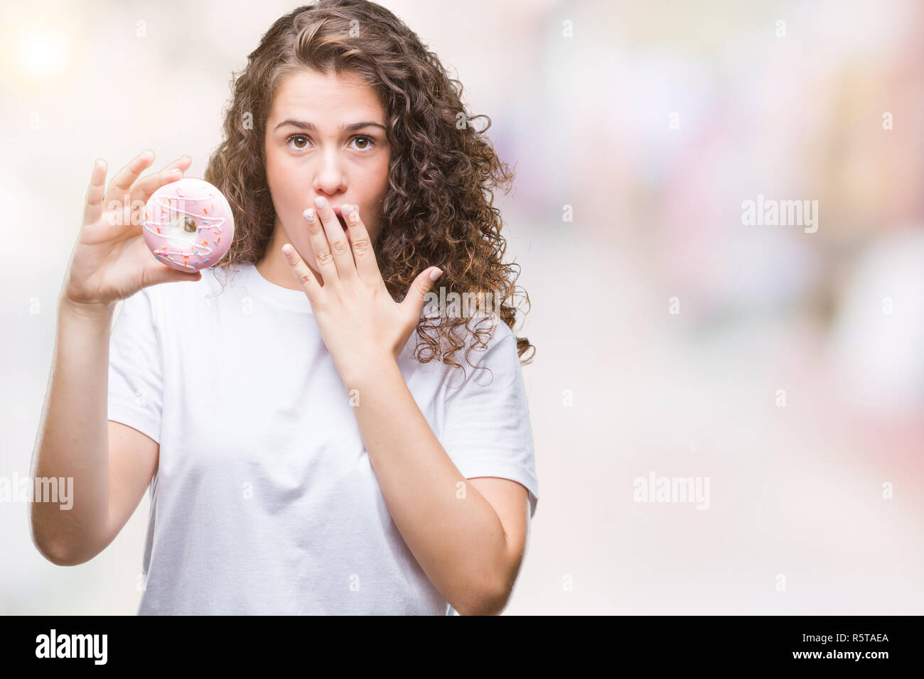Young brunette girl eating donut over isolated background cover mouth ...