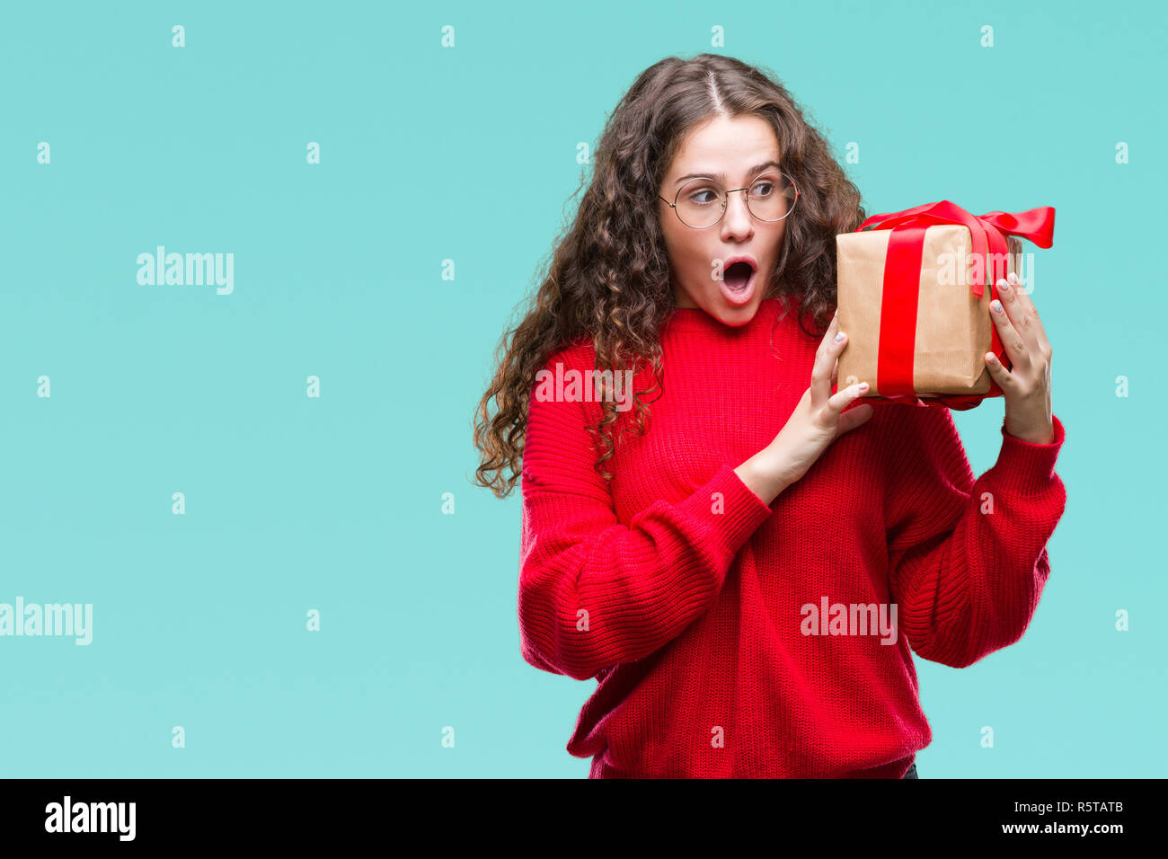 Young brunette girl holding a gift over isolated background scared in ...
