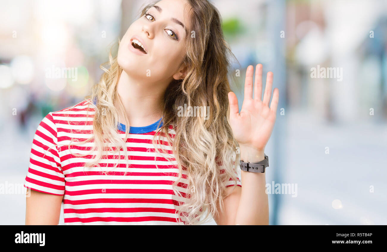 Beautiful young blonde woman over isolated background Waiving saying ...