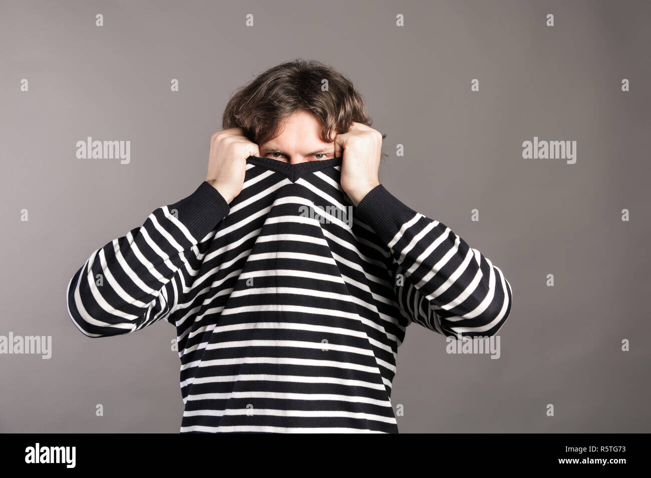 Portrait of young man with dark curly hair pulling her sweater over ...