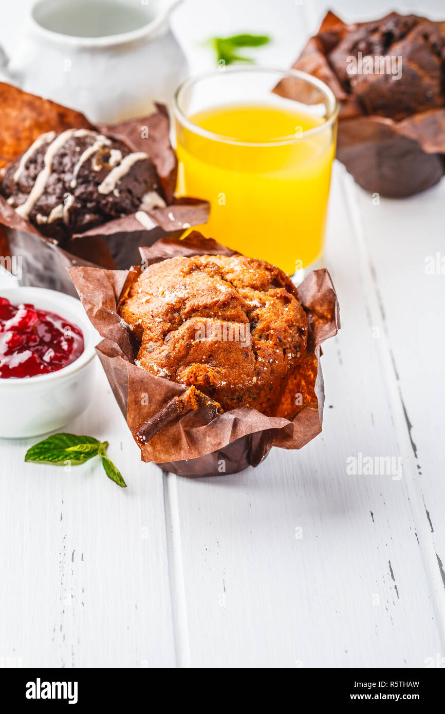 Different types of muffins on a white table with juice and milk for ...
