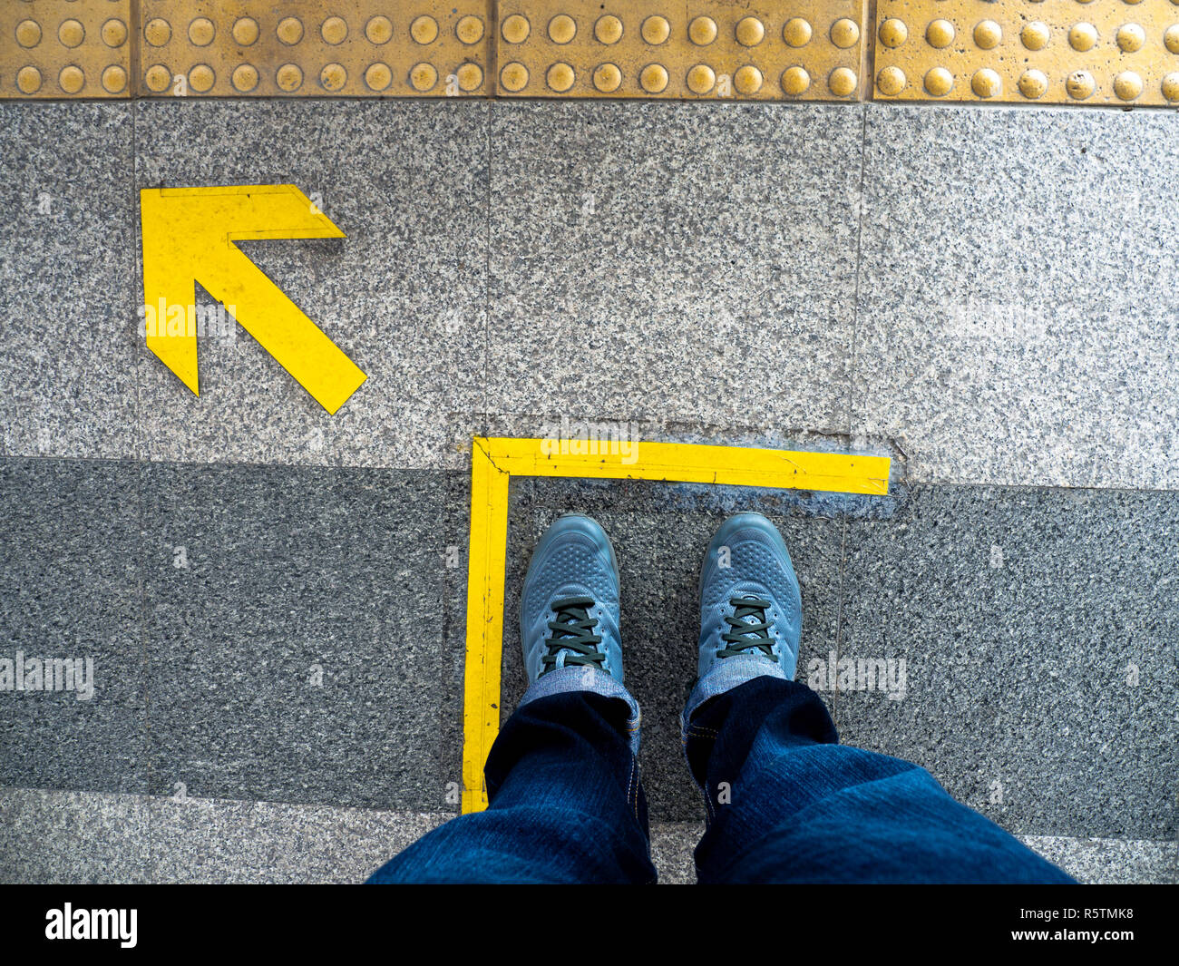 Top view of man feet standing over Arrow symbol on subway platform ...