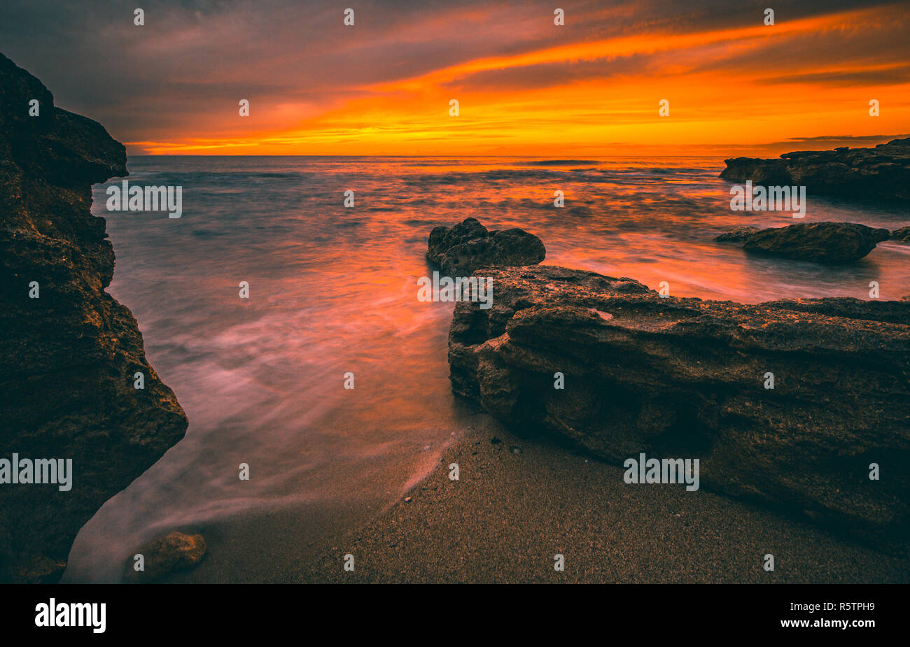 Sunset at the beach with rocks and waves Stock Photo - Alamy