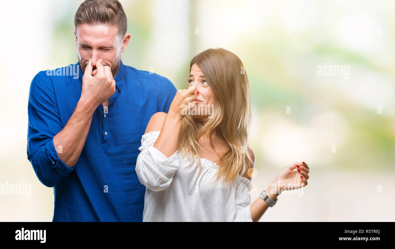 Young couple in love over isolated background smelling something stinky ...
