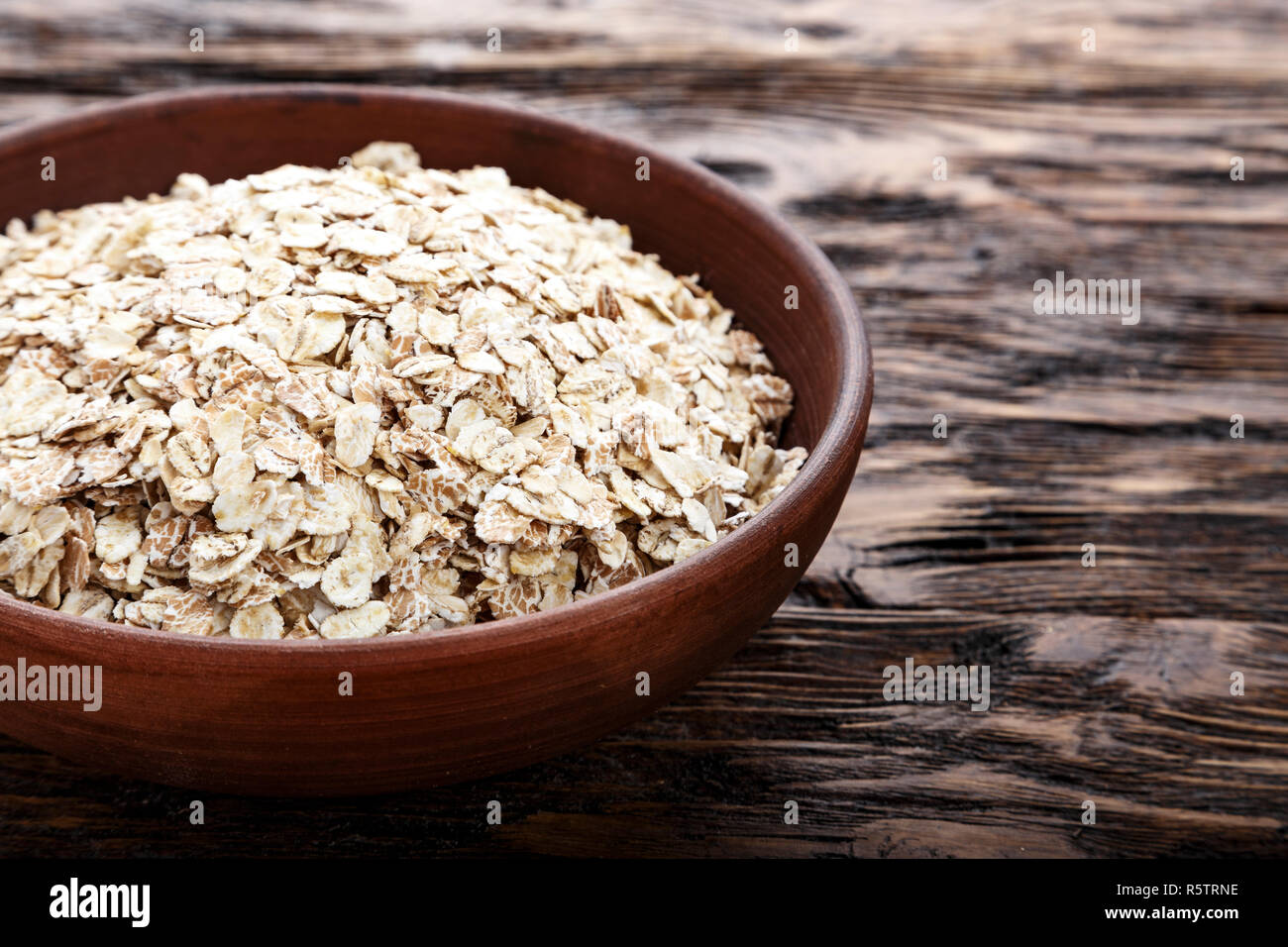 Raw oatmeal flakes in a clay plate on wooden background. healthy ...
