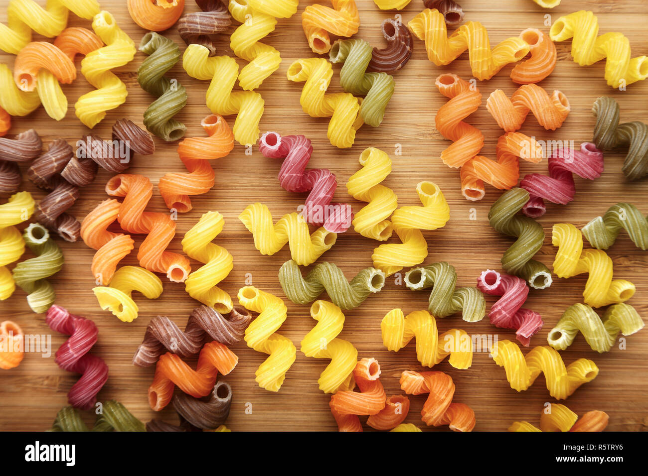 Uncooked multi colored pasta scattered as background on wooden ...