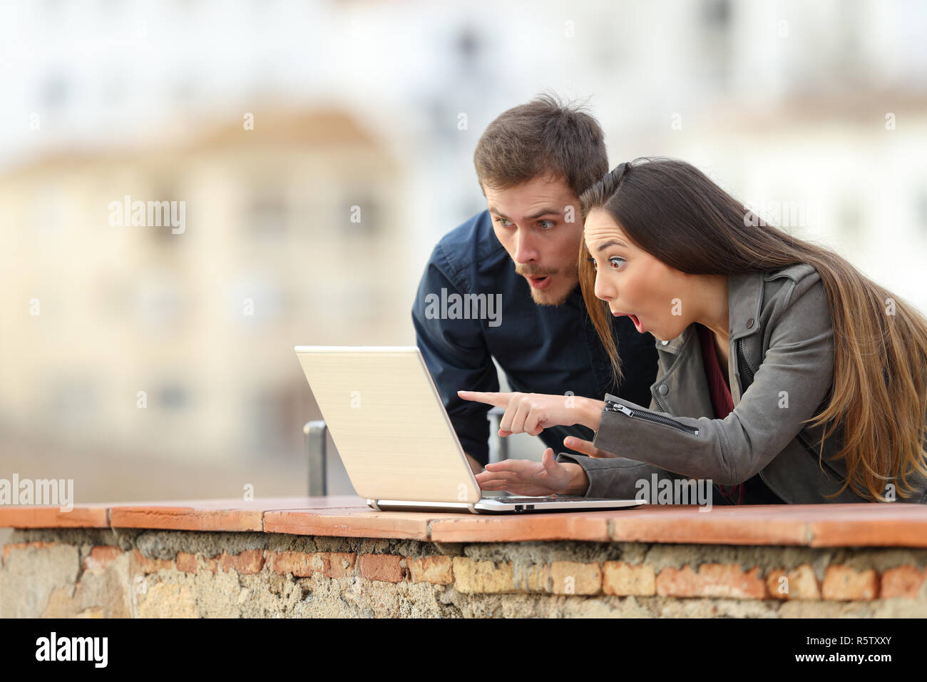 Surprised couple checking laptop content in a balcony with a town in ...