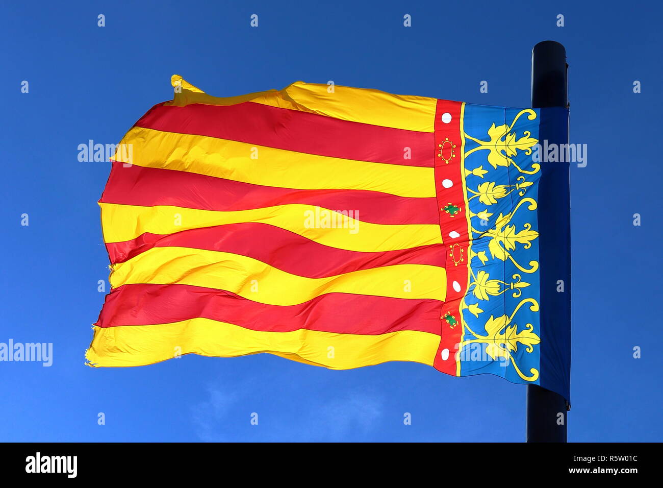 Flag of Valencia, Spain, waving in the wind in front of a blue sky ...
