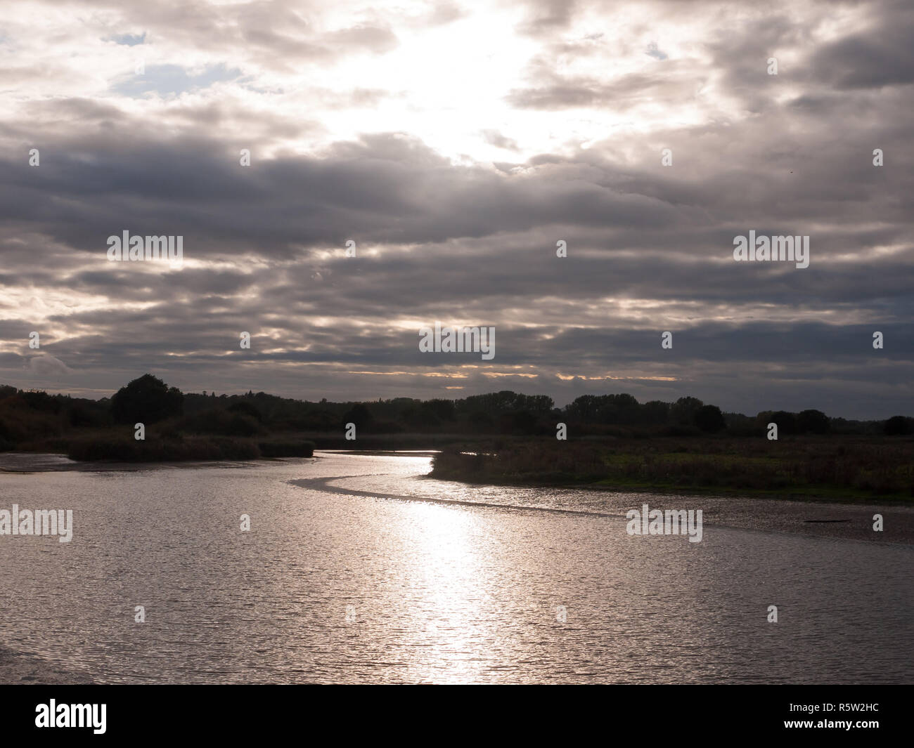 sun setting through dramatic clouds and onto lake river stream water ...