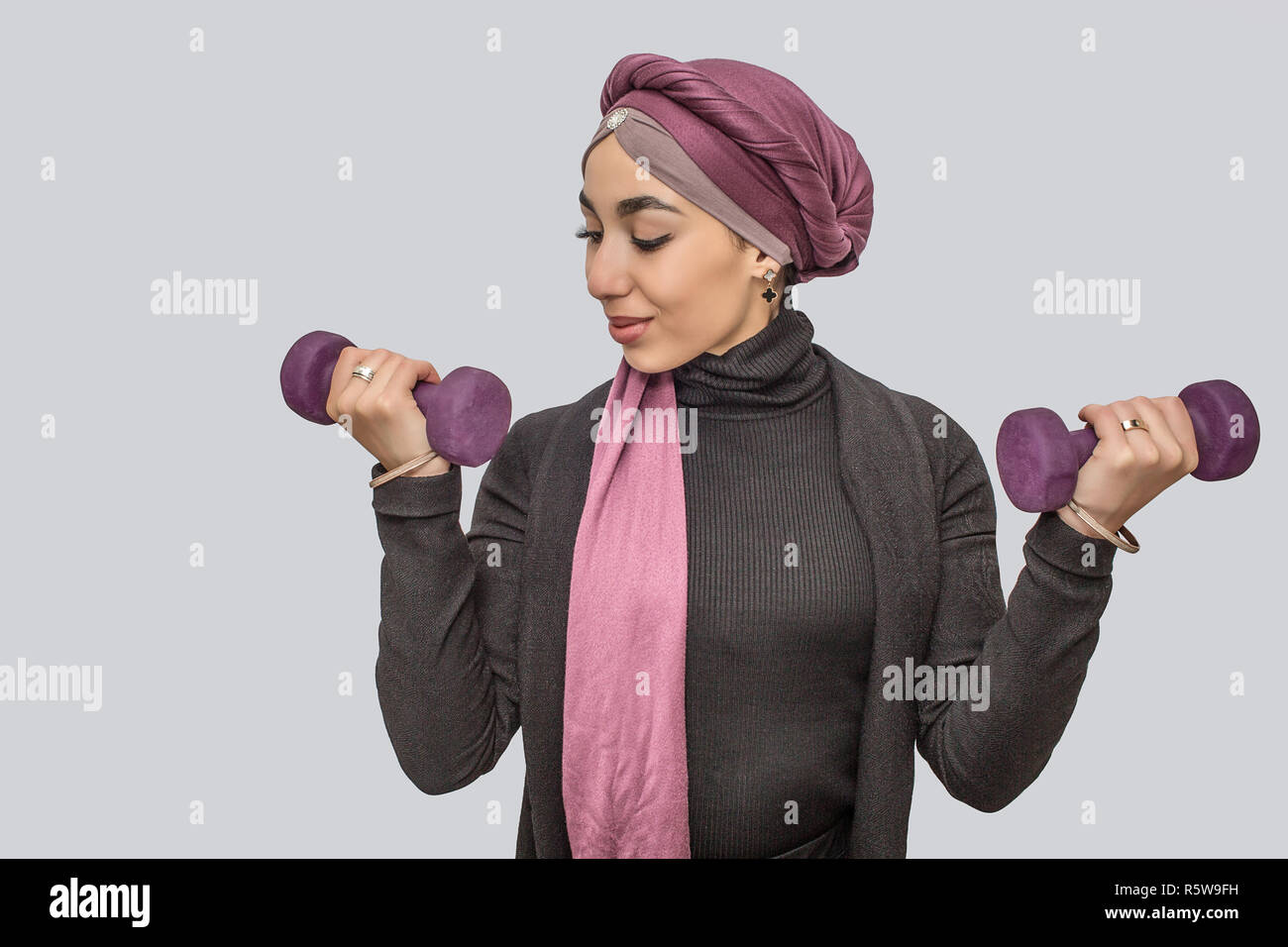 Strong young arabian woman exercising with dumbbells. She looks at one ...