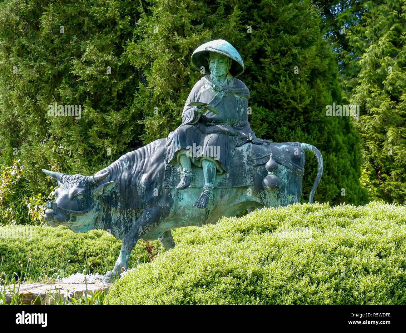 Sculpture of a Japanese man sitting on the back of a bull reading a ...