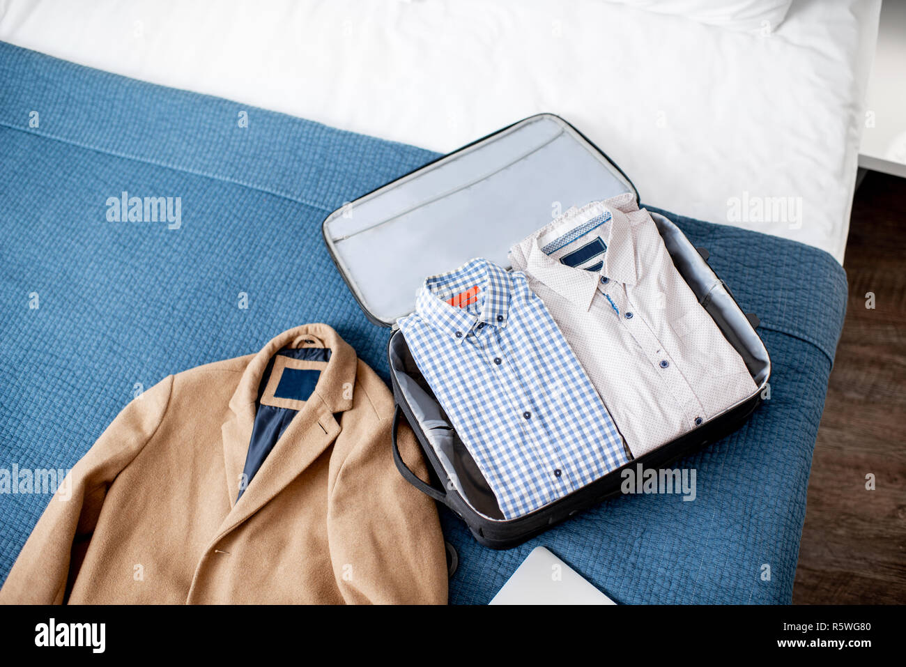 Suitcase full of clothes with coat on the bed of the hotel room or ...