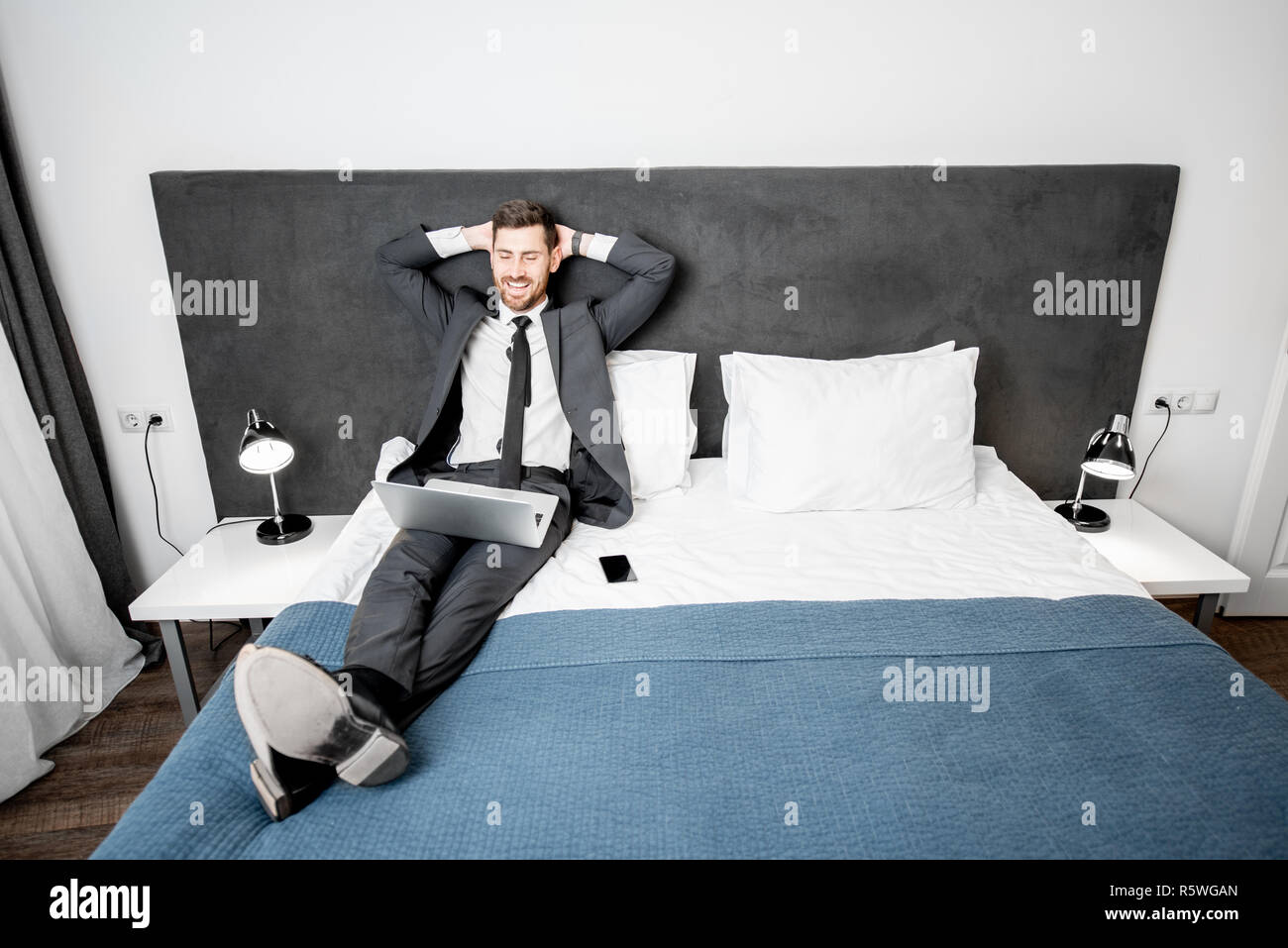 Relaxed businessman lying on the bed during his work with laptop at the ...