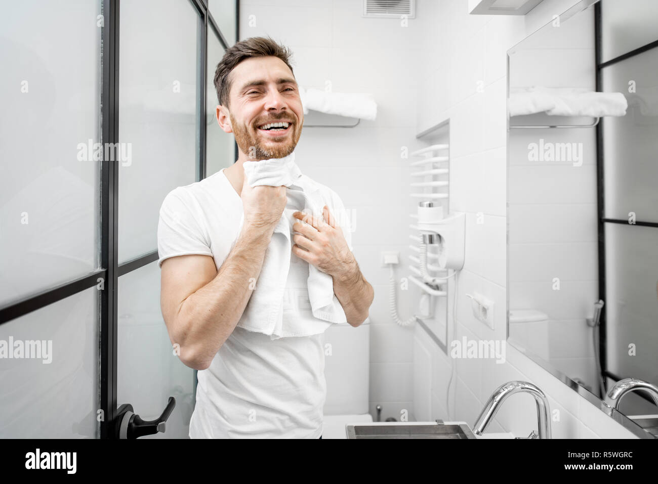 Portrait of a handsome man in white t-shirt drying his face with towel ...