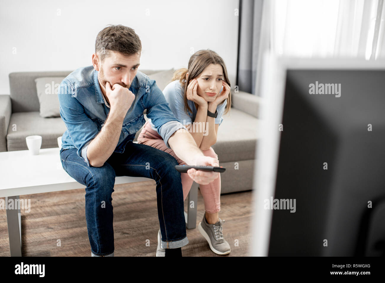 Young couple with unhappy faces watching boring TV sitting together on ...