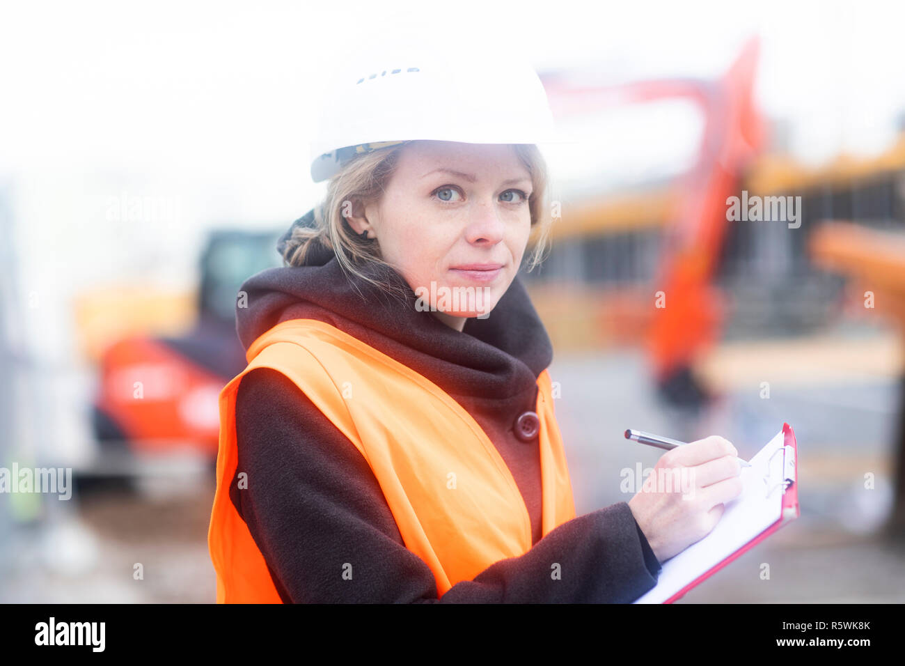 Portrait of a woman wearing a hard hat writing on a clipboard Stock ...