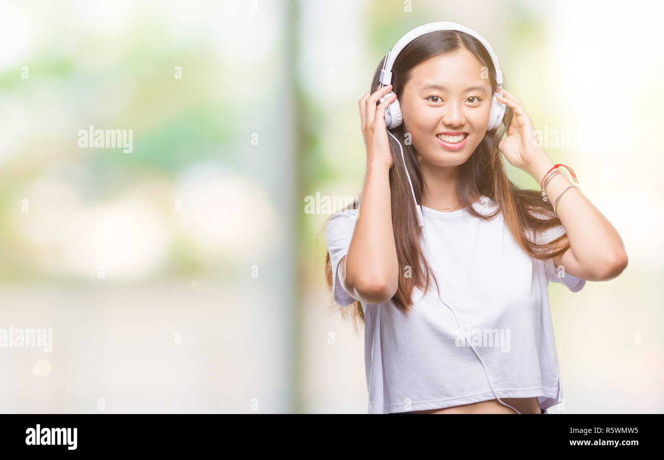 Young asian woman listening to music wearing headphones isolated ...