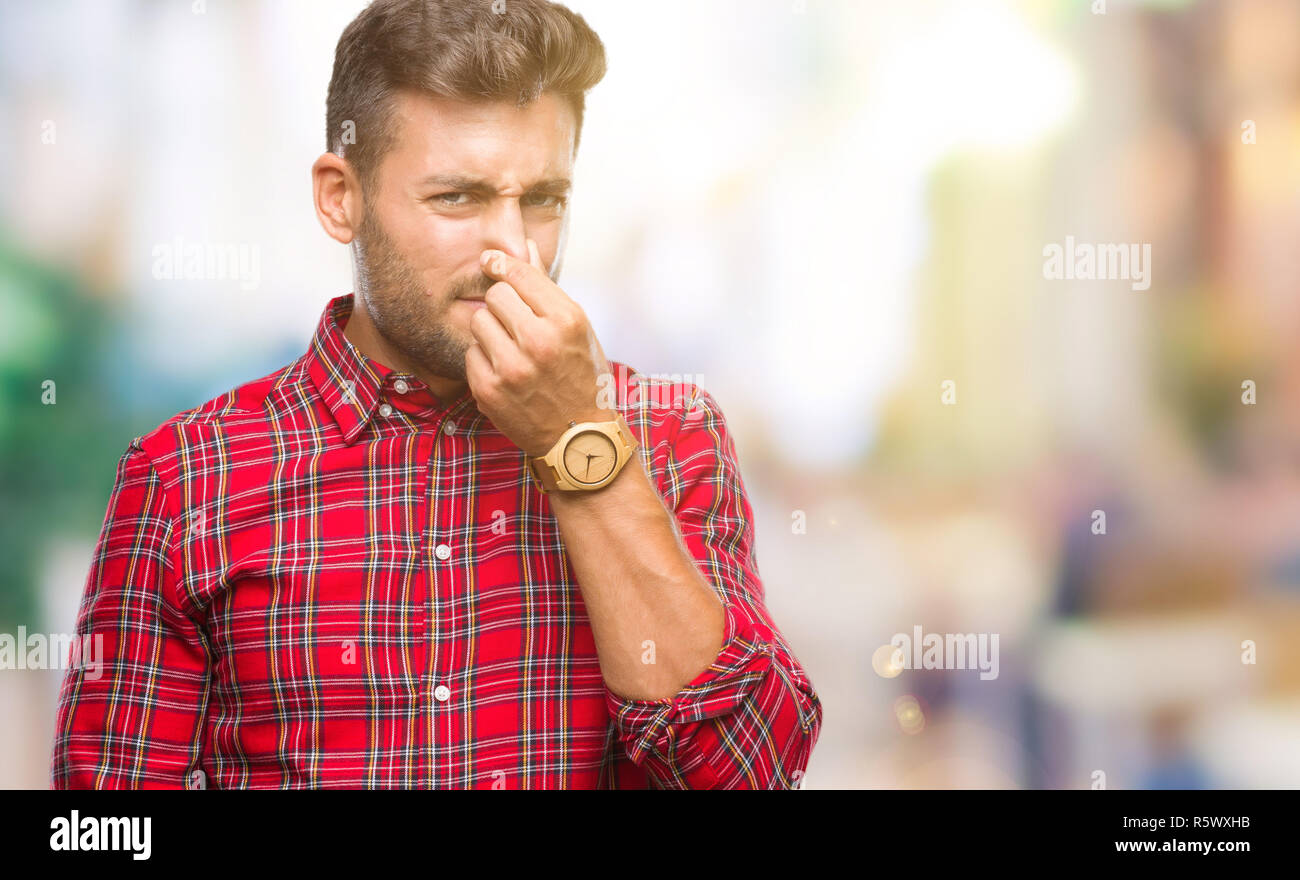 Young handsome man over isolated background smelling something stinky ...