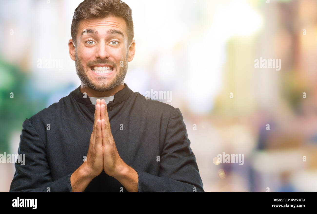 Young catholic christian priest man over isolated background praying ...