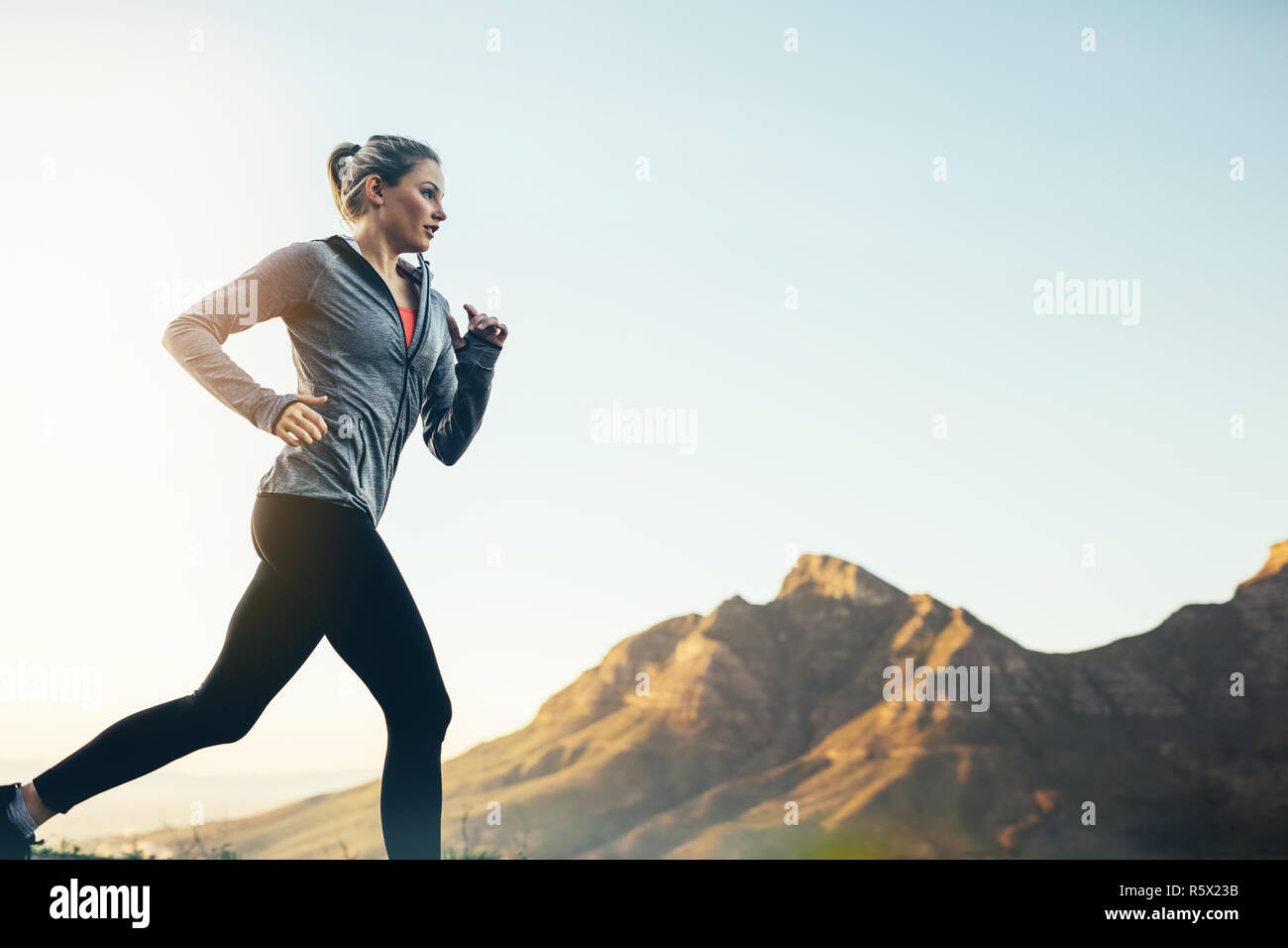 Side view of a fitness woman sprinting on road with hills in the ...