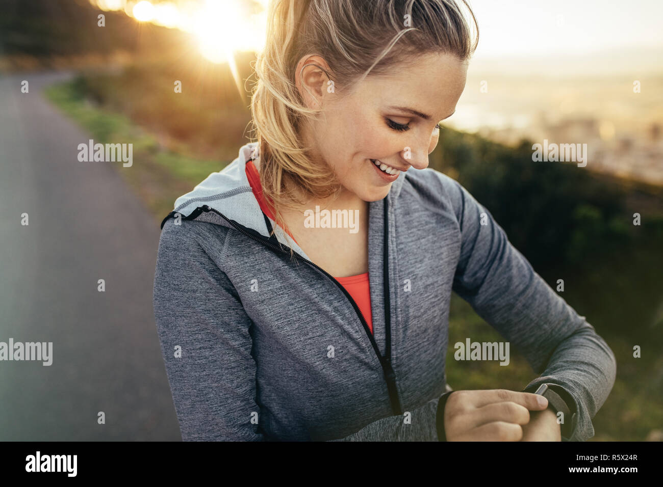 Smiling fitness woman setting a timer in her wrist watch standing ...